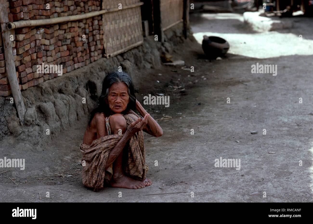 Old woman squats in front of a simple house on a street Stock Photo - Alamy