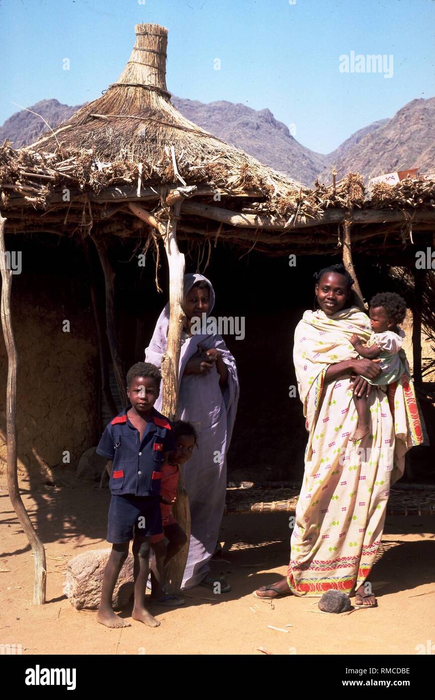 Sudanese women with their children in front of their thatched huts ...