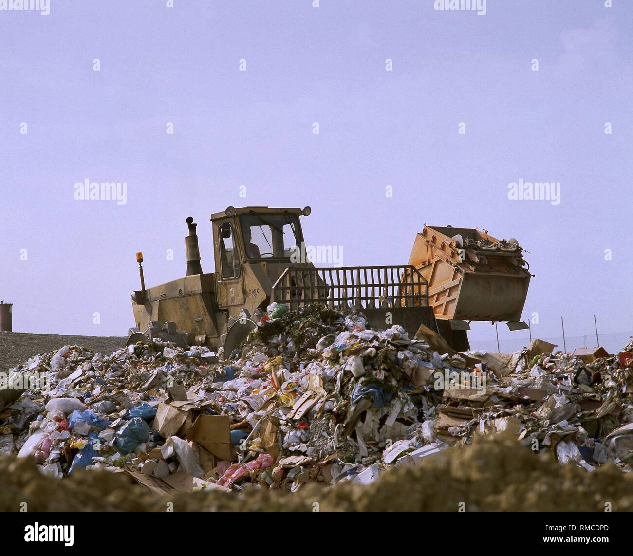 A bulldozer when moving waste on a landfill, in the background a ...