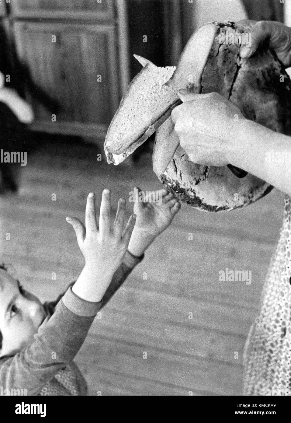 A child grabs at a slice of bread cut by a woman Stock Photo - Alamy