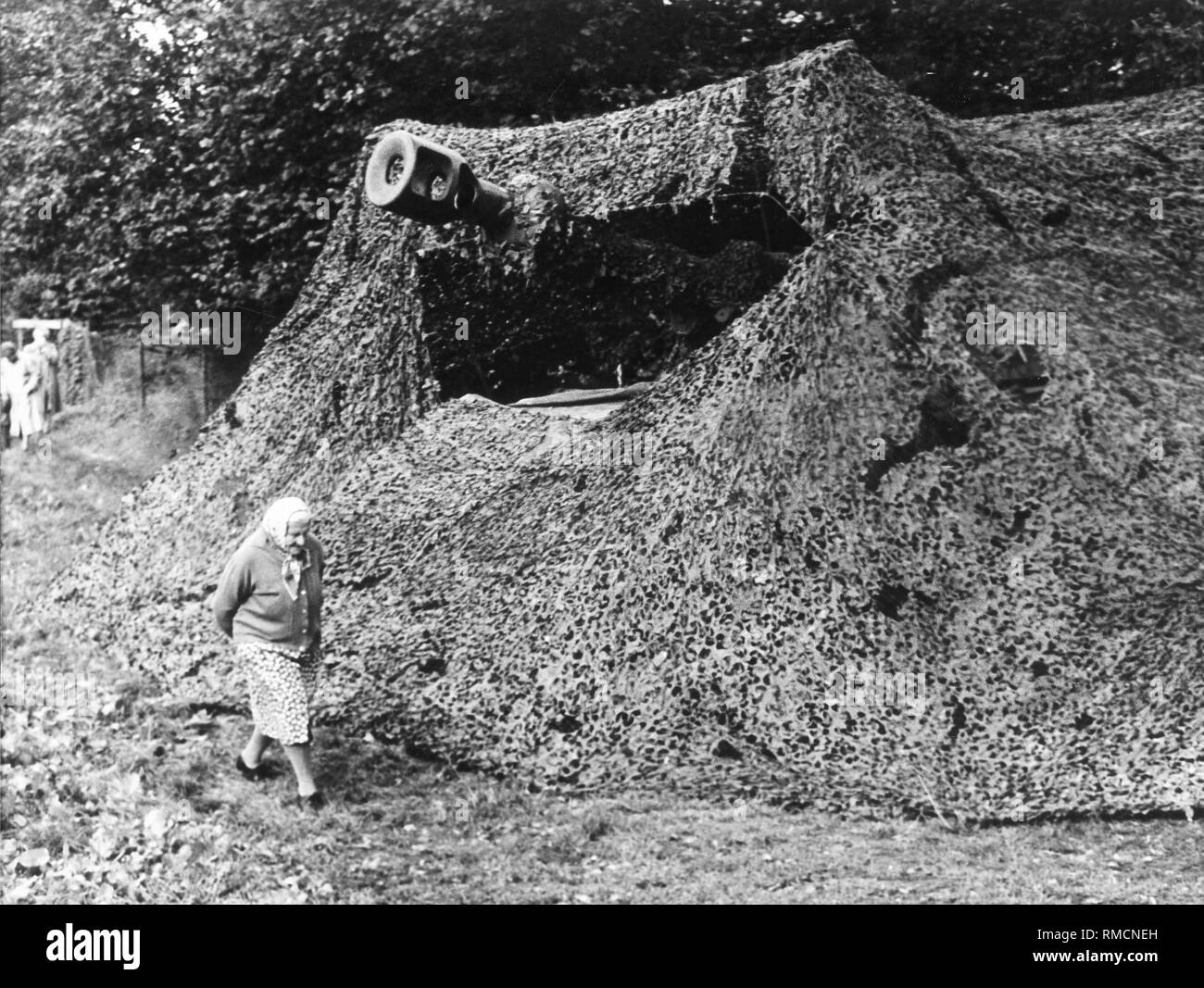 An old woman walks past a camouflaged firing position of an M 103 ...