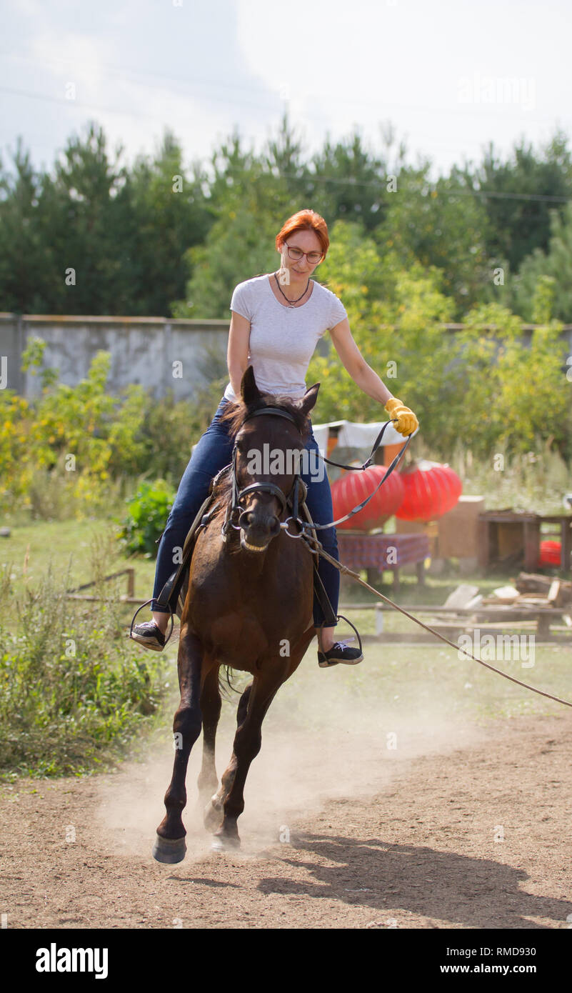 A redhead woman in glasses riding a horse in nature Stock Photo - Alamy
