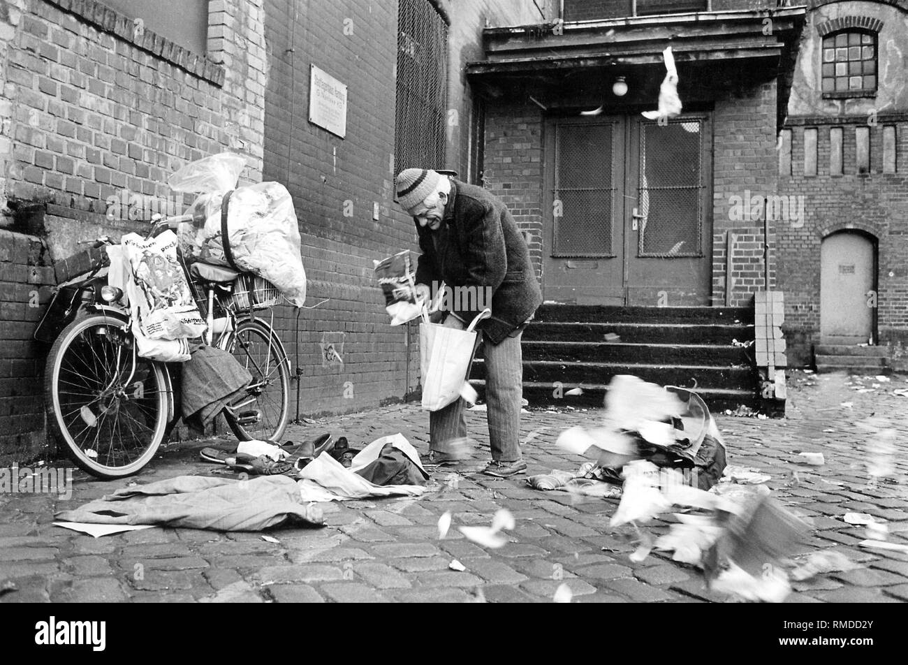 A homeless man rummages in a paper bag in front of a house entrance ...