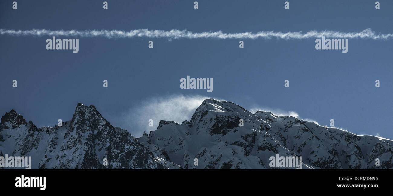 Panoramic blue view of wind blowing over snow capped mountain peaks ...