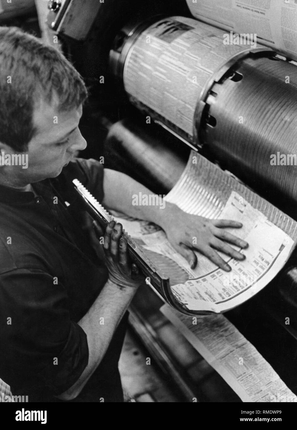A pressman lifts a semicircular printing plate into a rotary printing ...