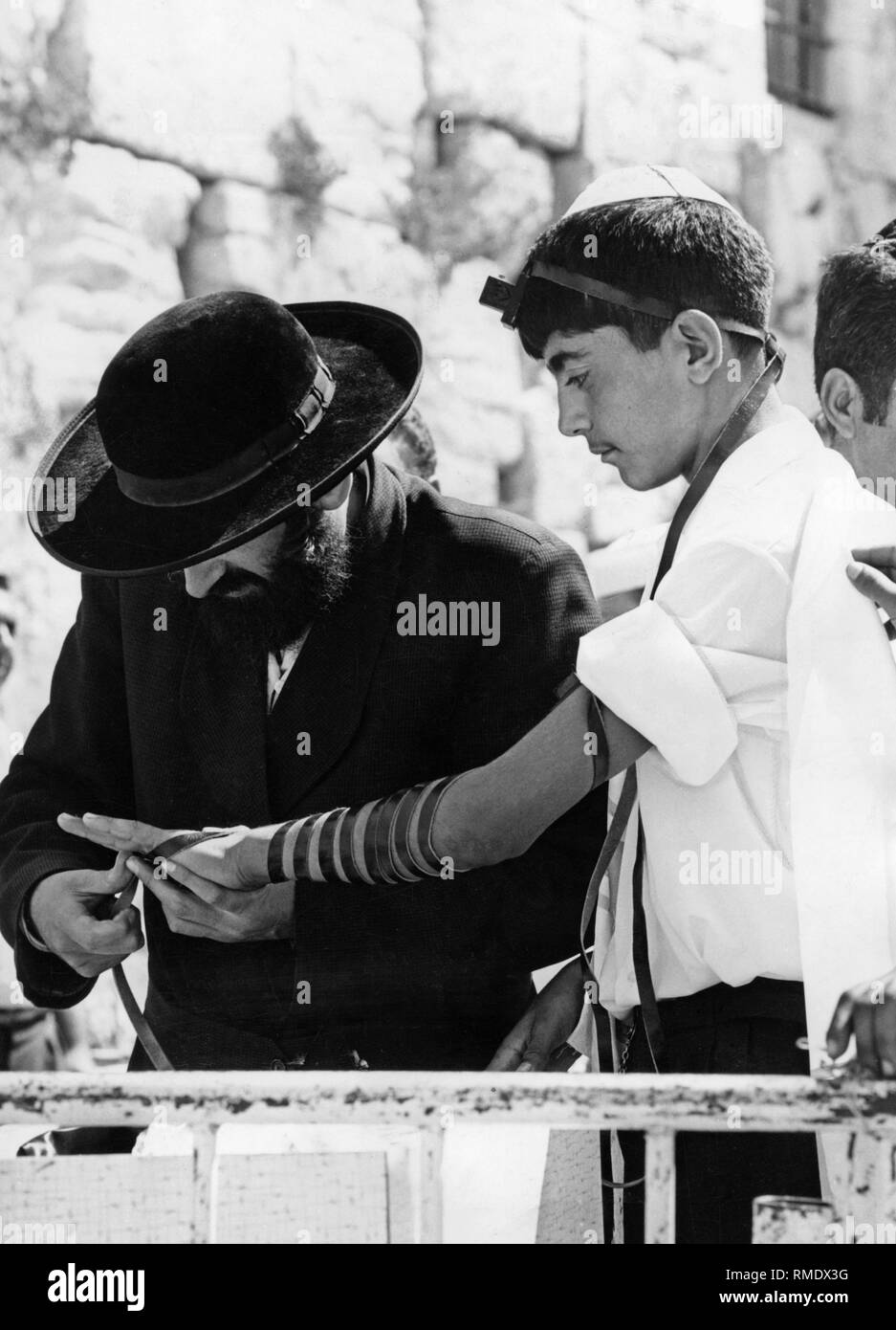 A rabbi helps out a boy with a tefillin. The tefillin, which is a small ...