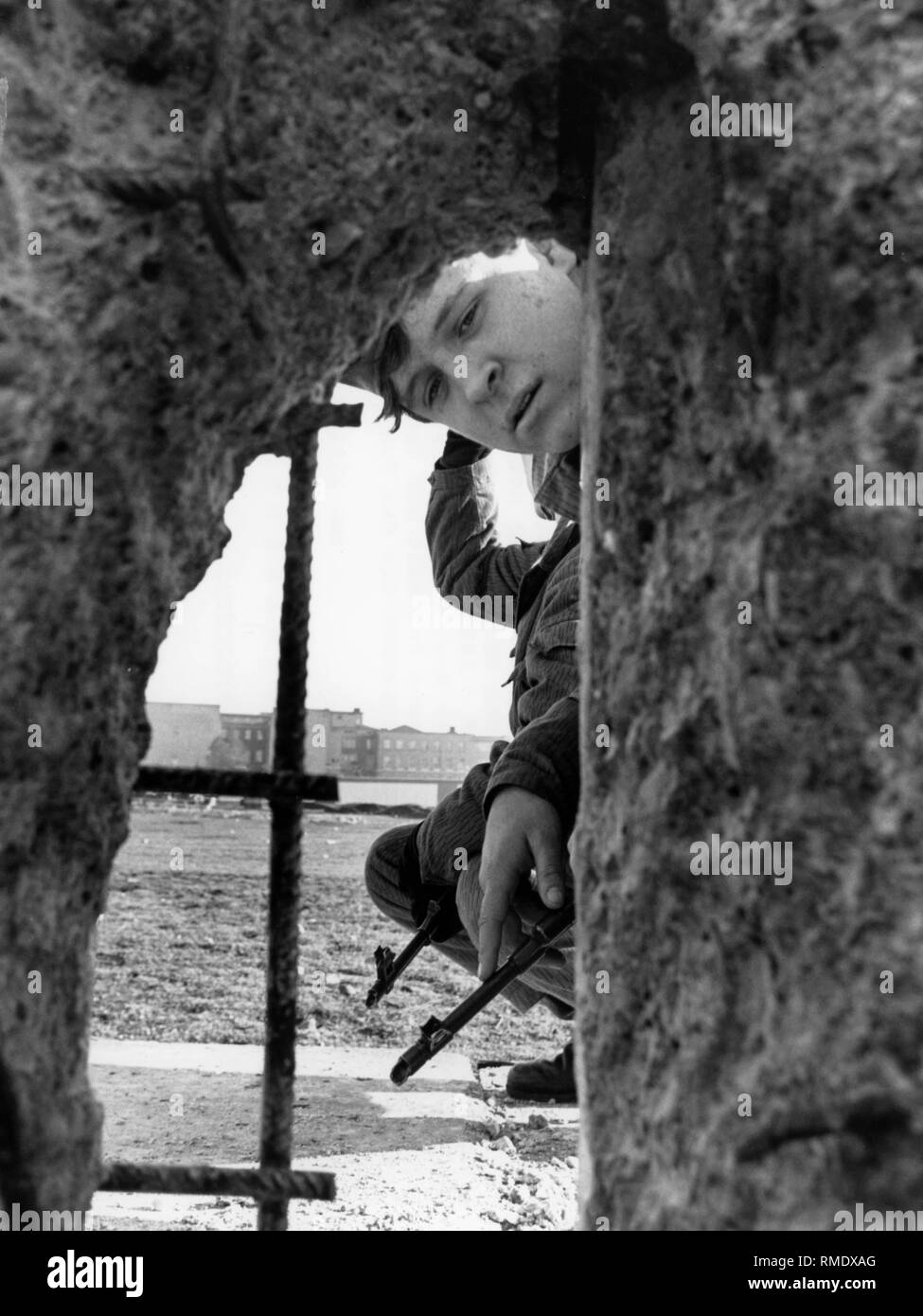 A member of the border troop looks through a hole in the Berlin Wall ...