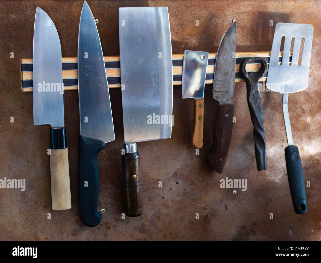 Various kitchen utensils on a magnetic knife block against a rusty ...