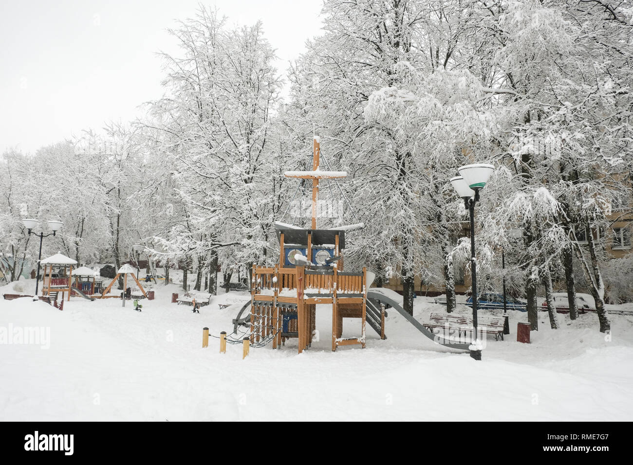 a playground in a park in the city covered by snow in winter. Trees ...