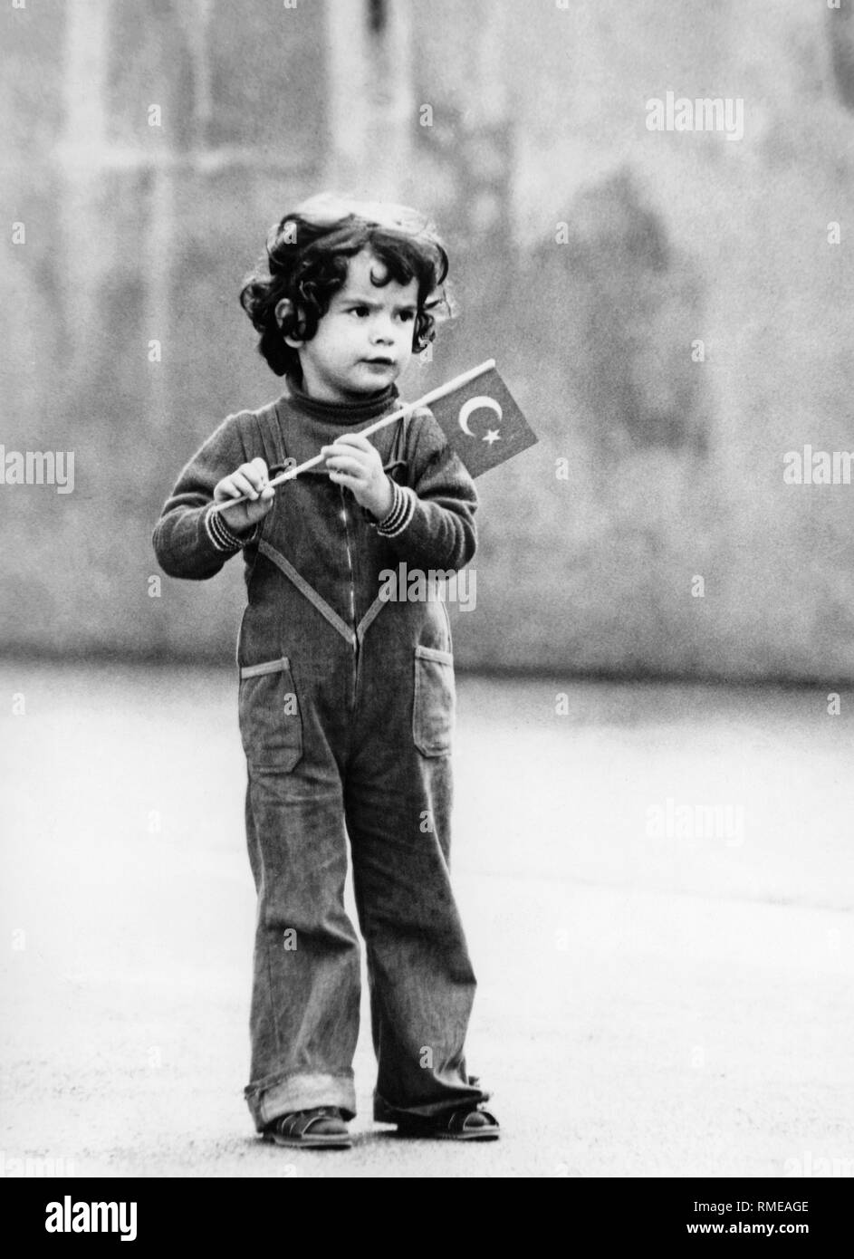 A guest worker child holds a small, Turkish national flag in his hand ...