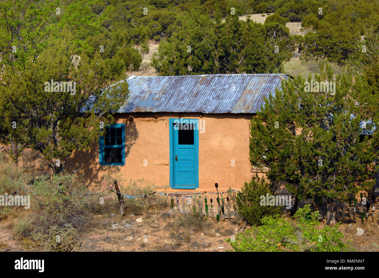Small adobe home has turquoise painted door and tin roof. A unique fence, made of old glass ...