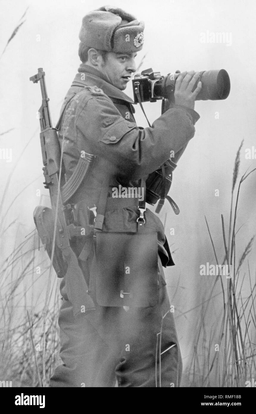 A GDR border guard with gun and camera at the German-German border near ...