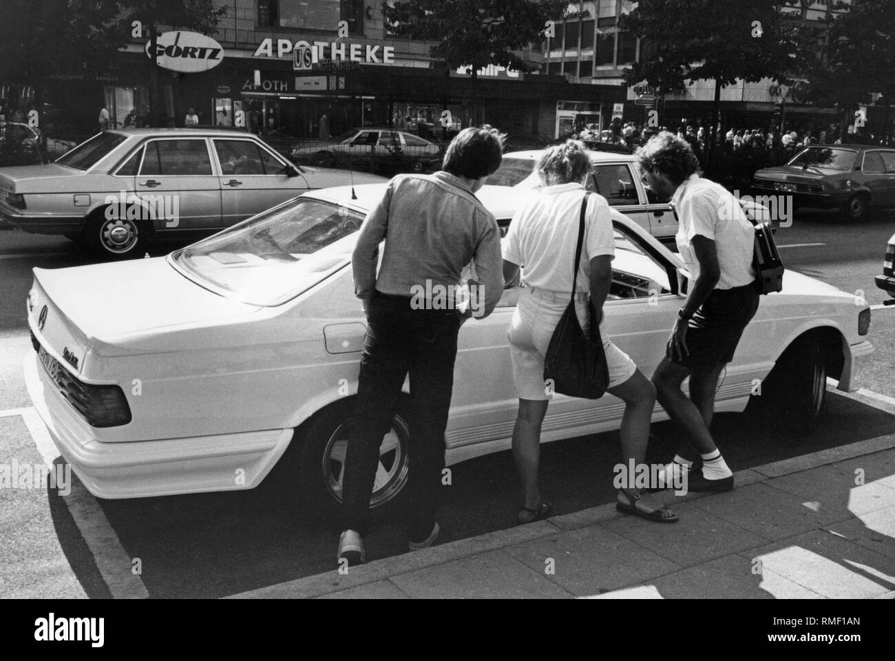 Three passers-by look at a Mercedes 500 SEC (C126 series) with AMG rims ...