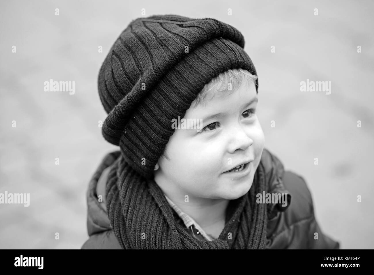 Cute blond boy in black hat and blue parka walking on street. Closeup ...