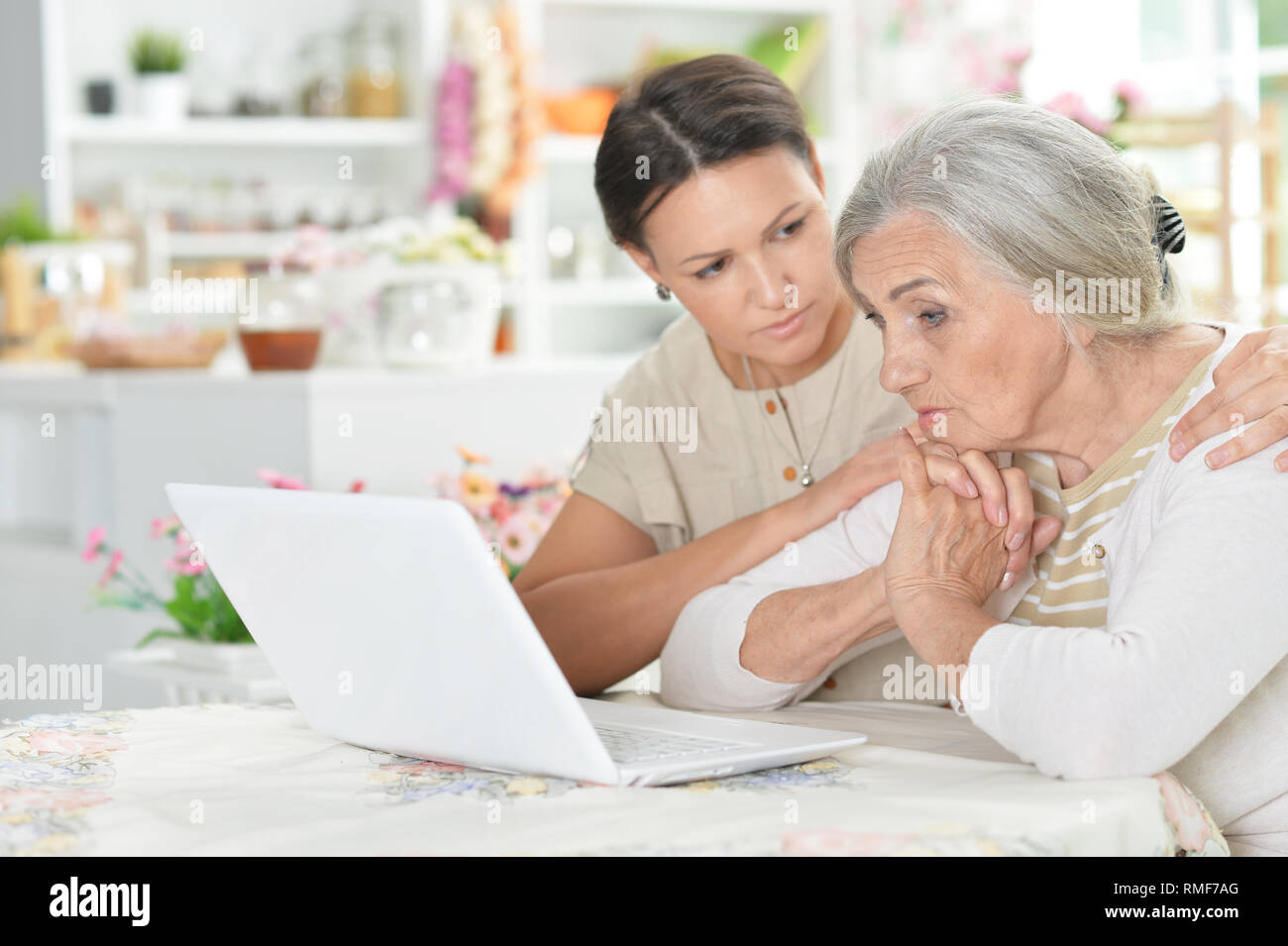 Portrait of sad mother and daughter sitting at table with laptop at ...