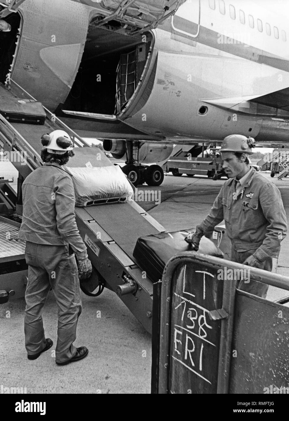 Apron staff load luggage items into the hold of a passenger engine at ...