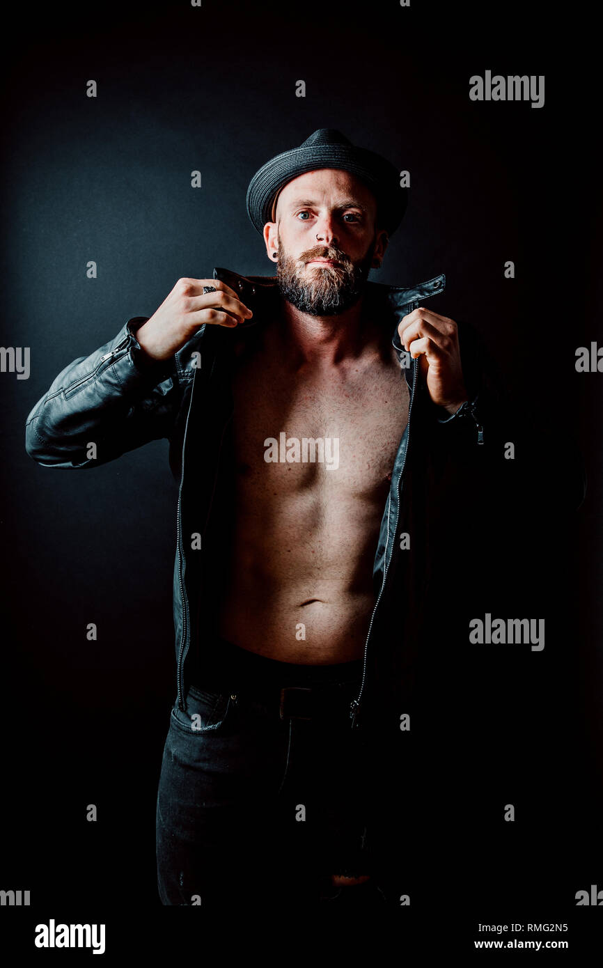 Shirtless cool hipster in hat adjusting leather jacket and looking at ...