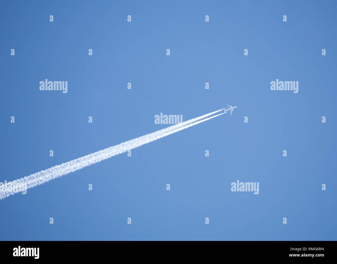 Large passenger jet flying high in clear blue sky, leaving long white ...