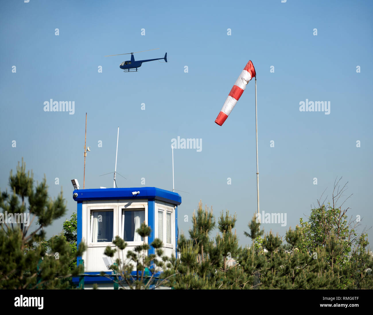 Small blue helicopter flies over an airfield weather station in summer ...