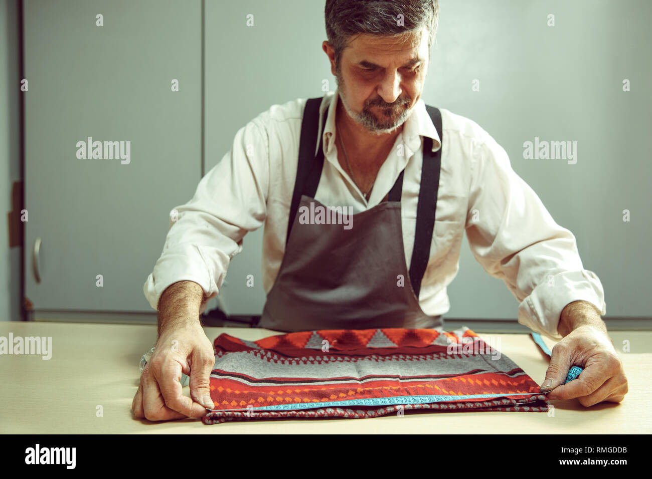 Closeup of tailors table with male hands tracing fabric making pattern ...