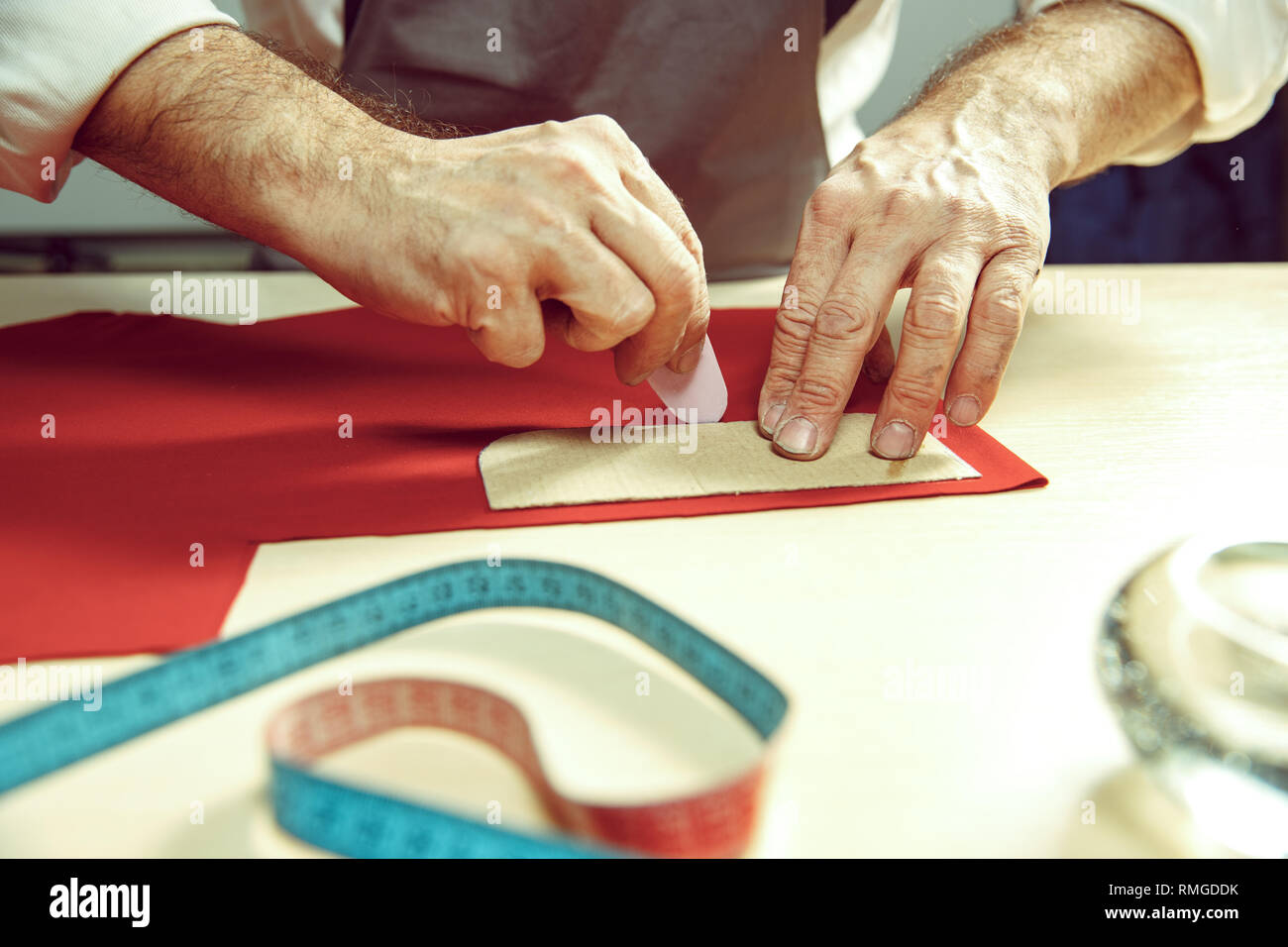 Closeup of tailors table with male hands tracing fabric making pattern ...