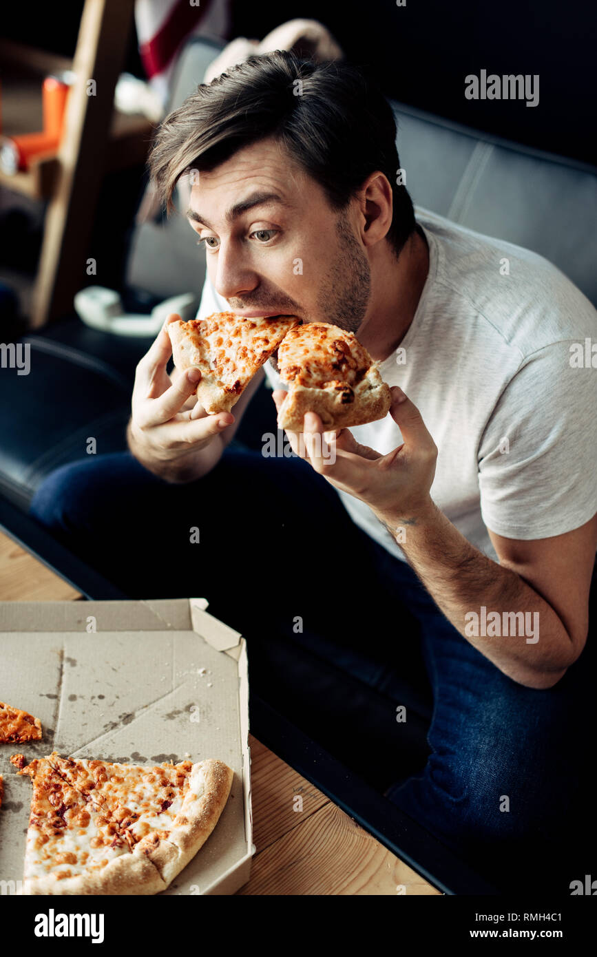 hungry man eating tasty pizza in living room Stock Photo - Alamy