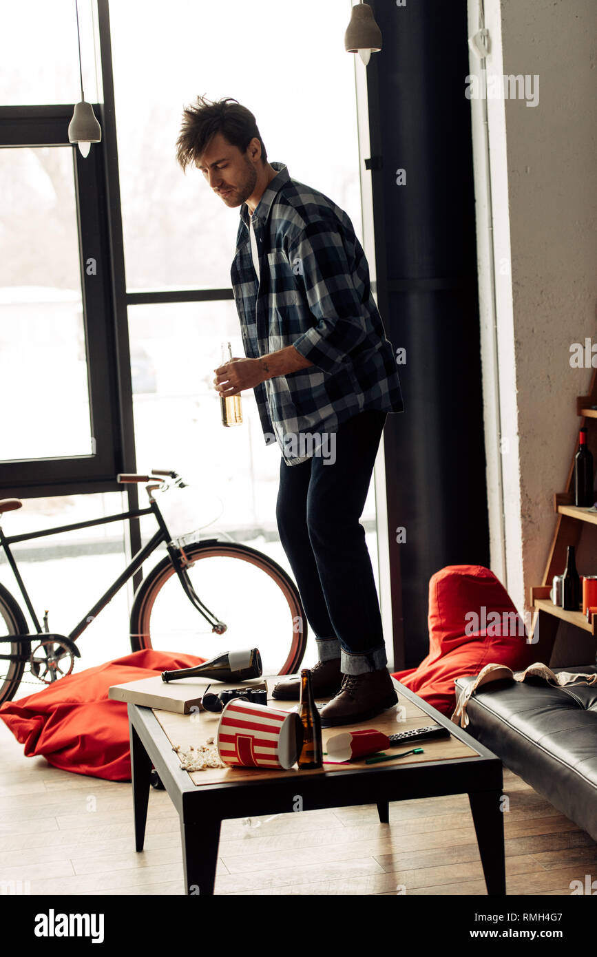 drunk sleepy man standing on coffee table and holding drink after party ...