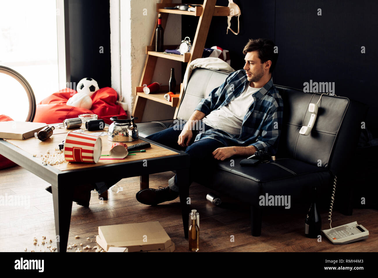drunk man sitting on sofa in messy living room after party Stock Photo ...