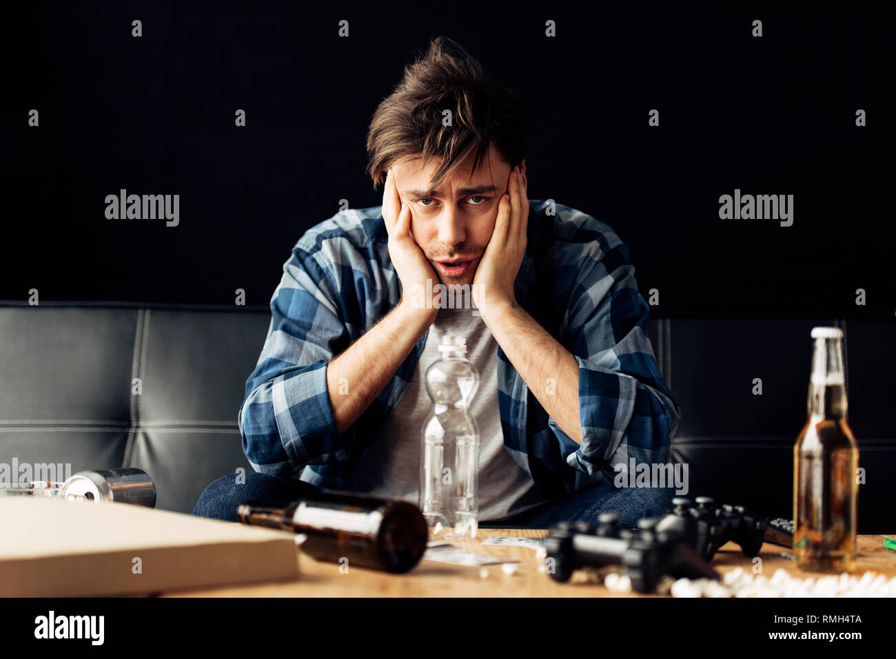 man suffering from hangover holding head near bottles at home Stock ...