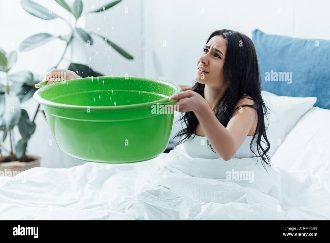 Upset girl in bed dealing with water damage and using basin Stock Photo ...