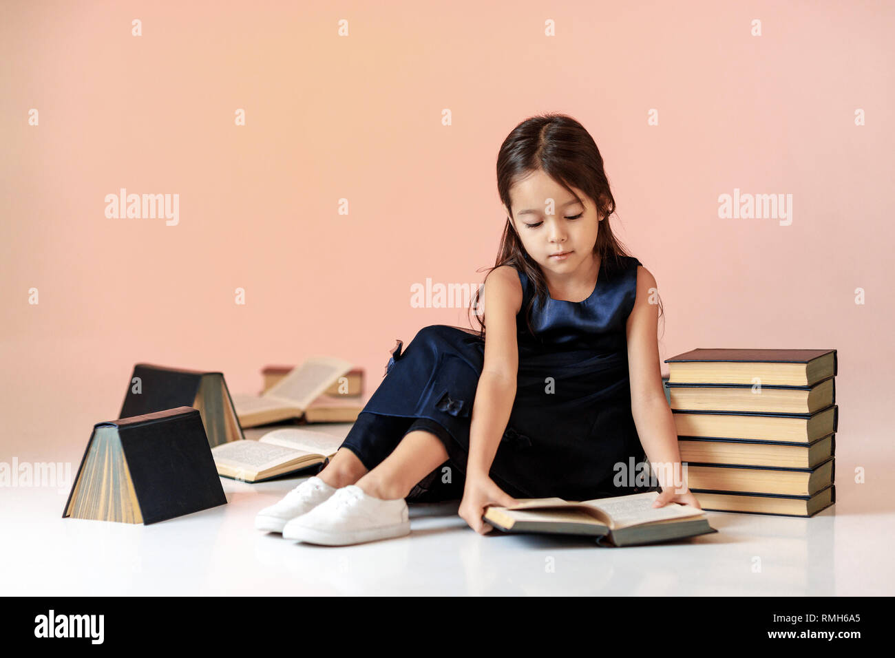 cute little girl in dark blue dress is reading a book. child and a lot ...