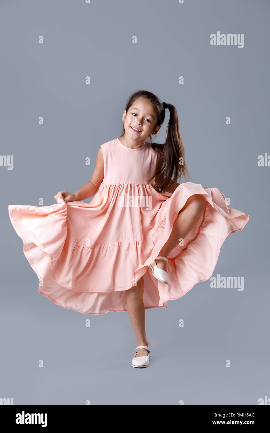 cute smiling little child girl in pink dress dancing on gray background ...
