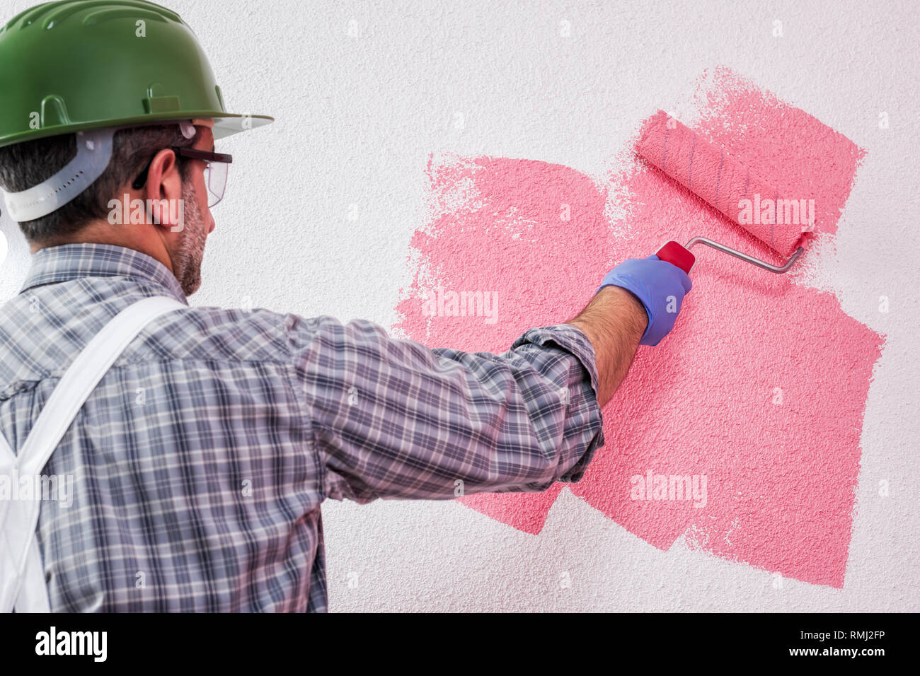 Caucasian house painter worker in white work overalls, with the roller ...