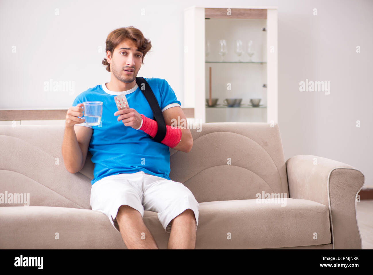 Young man with injured arm sitting on the sofa Stock Photo - Alamy