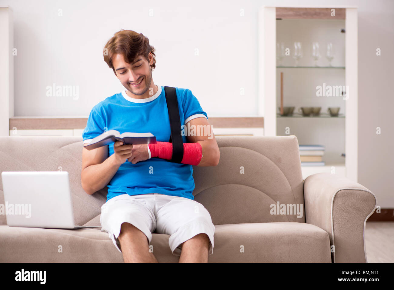 Young man with injured arm sitting on the sofa Stock Photo - Alamy