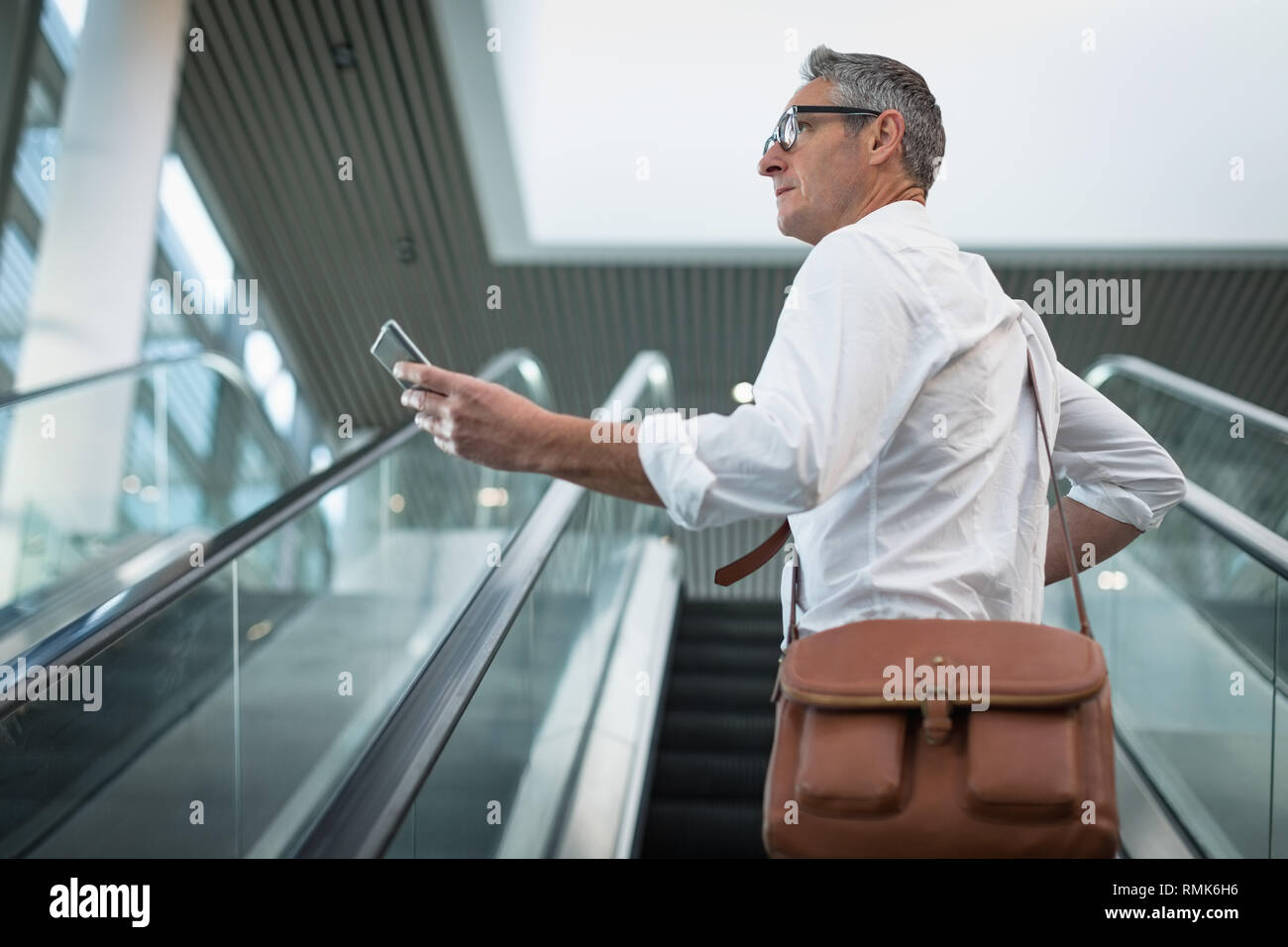 Businessman checking his mobile phone on the escalator Stock Photo - Alamy
