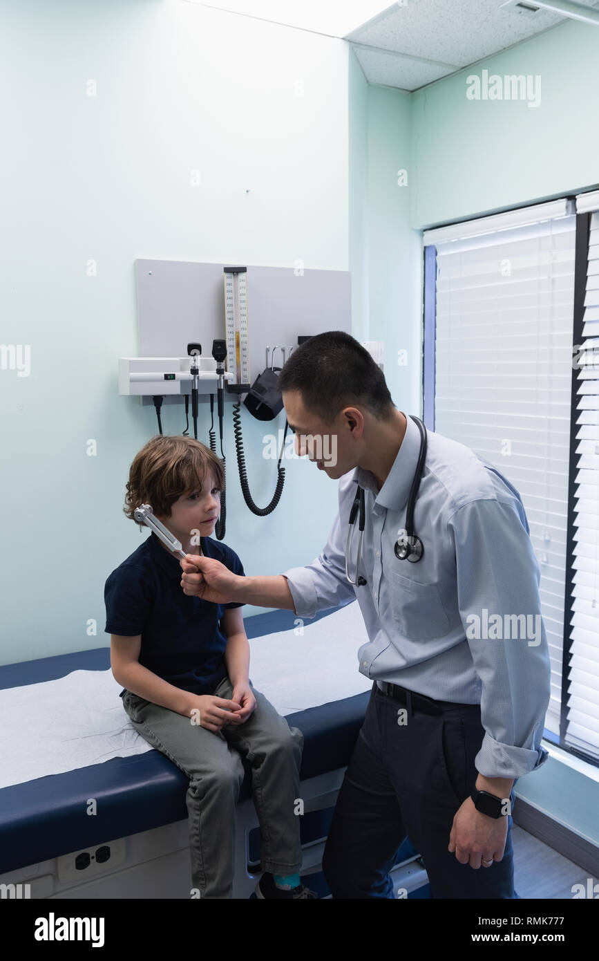 Young asian male doctor showing tuning fork to caucasian boy patient in ...