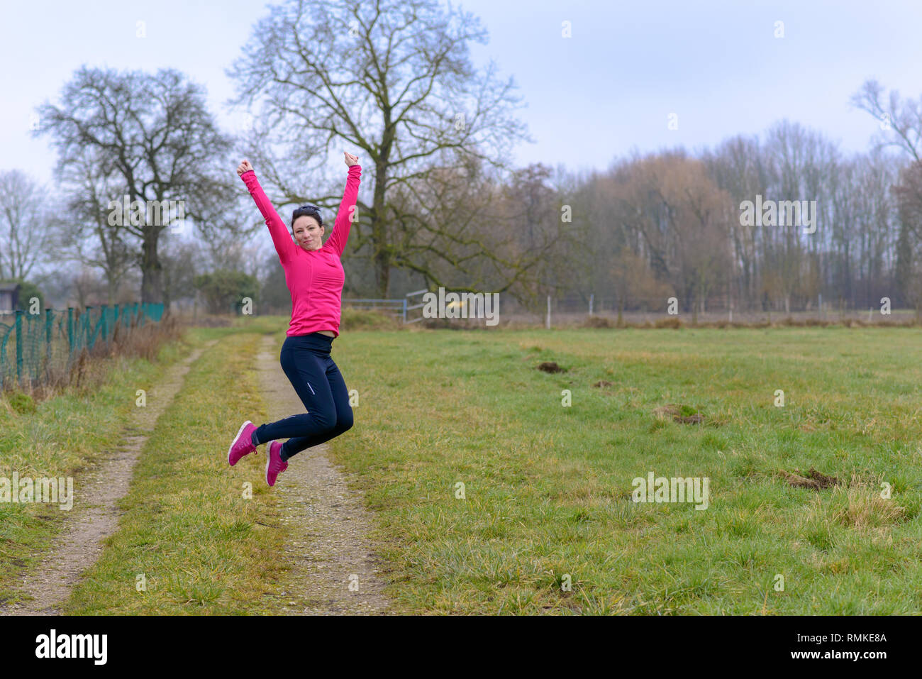 Agile athletic woman leaping in the air with her arms raised on a farm ...