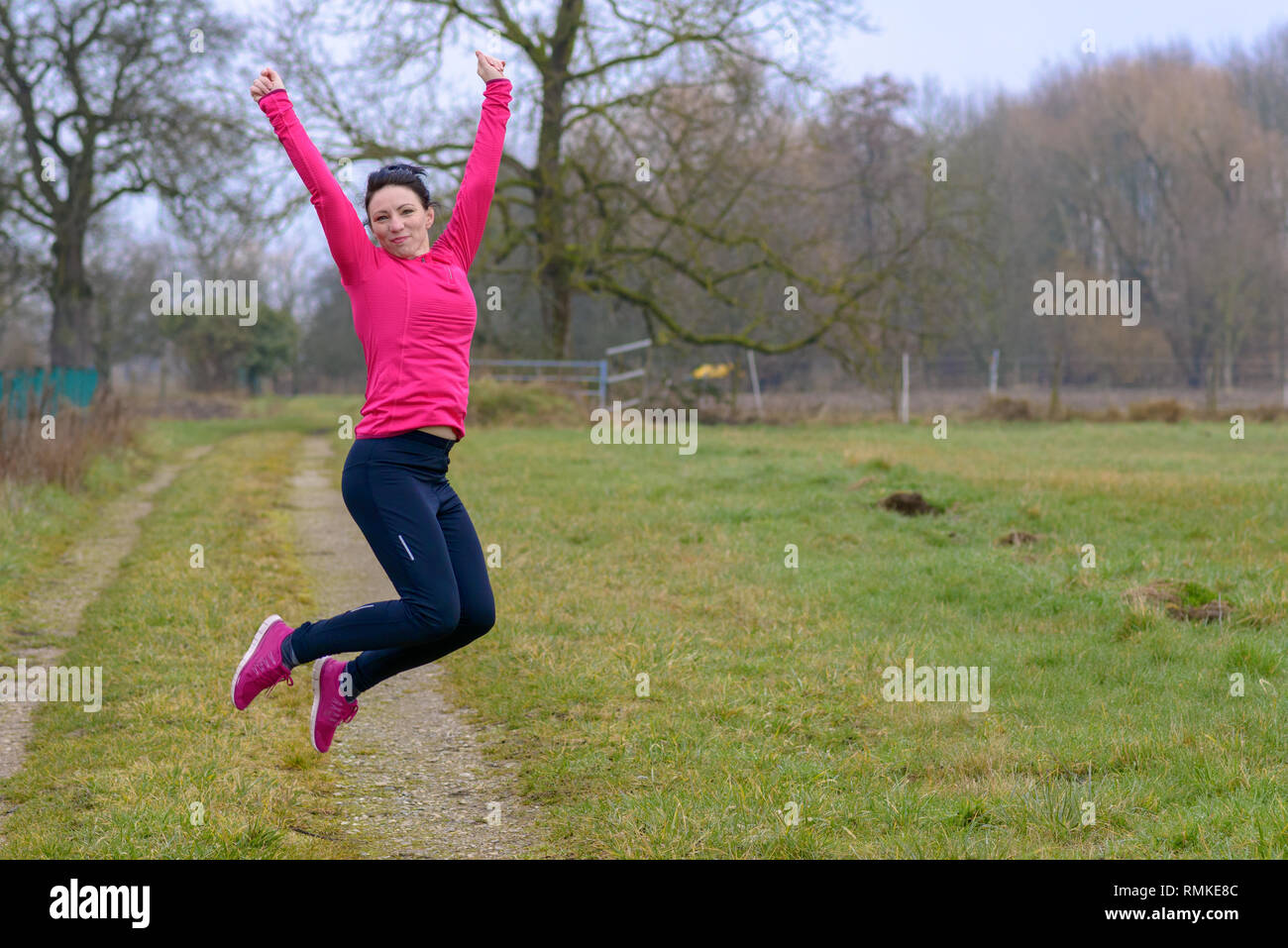 Agile athletic woman leaping in the air with her arms raised on a farm ...