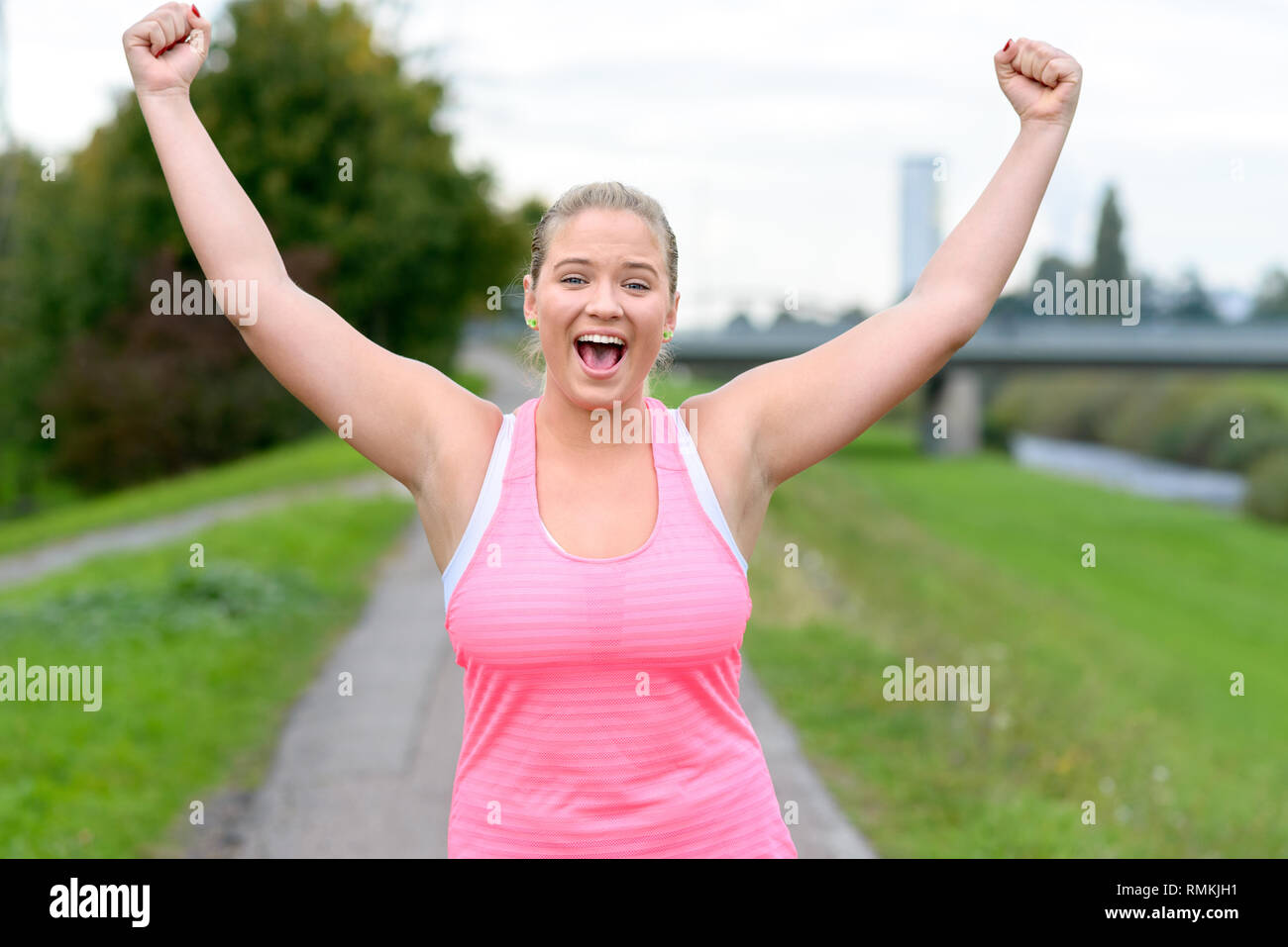 Outdoor portrait of young smiling woman raising hands while jogging ...