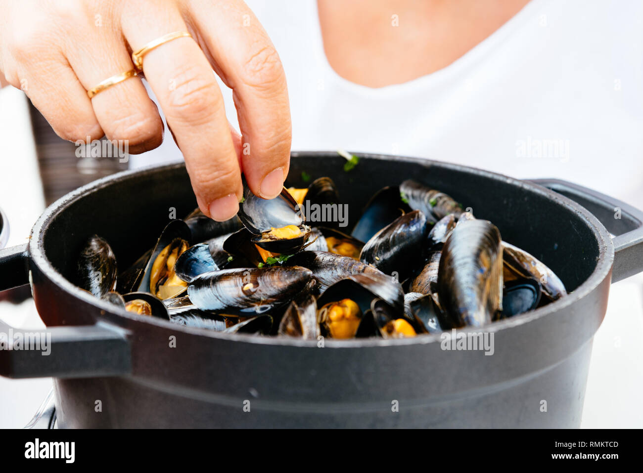 Close up of female hand taking steamed mussels with parsley, wine and ...