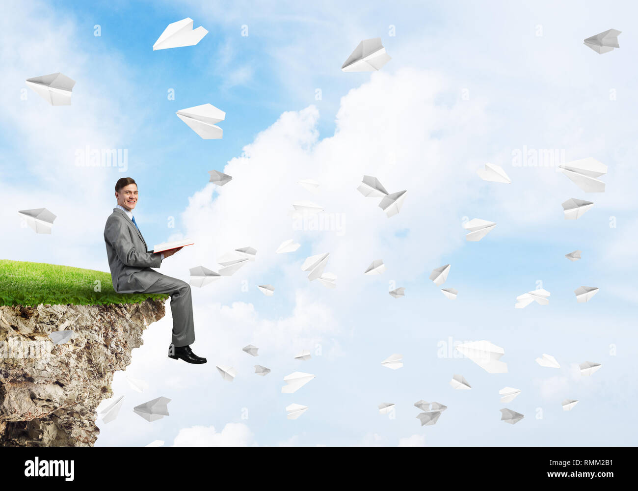 Man on edge reading book and paper planes flying in air Stock Photo - Alamy