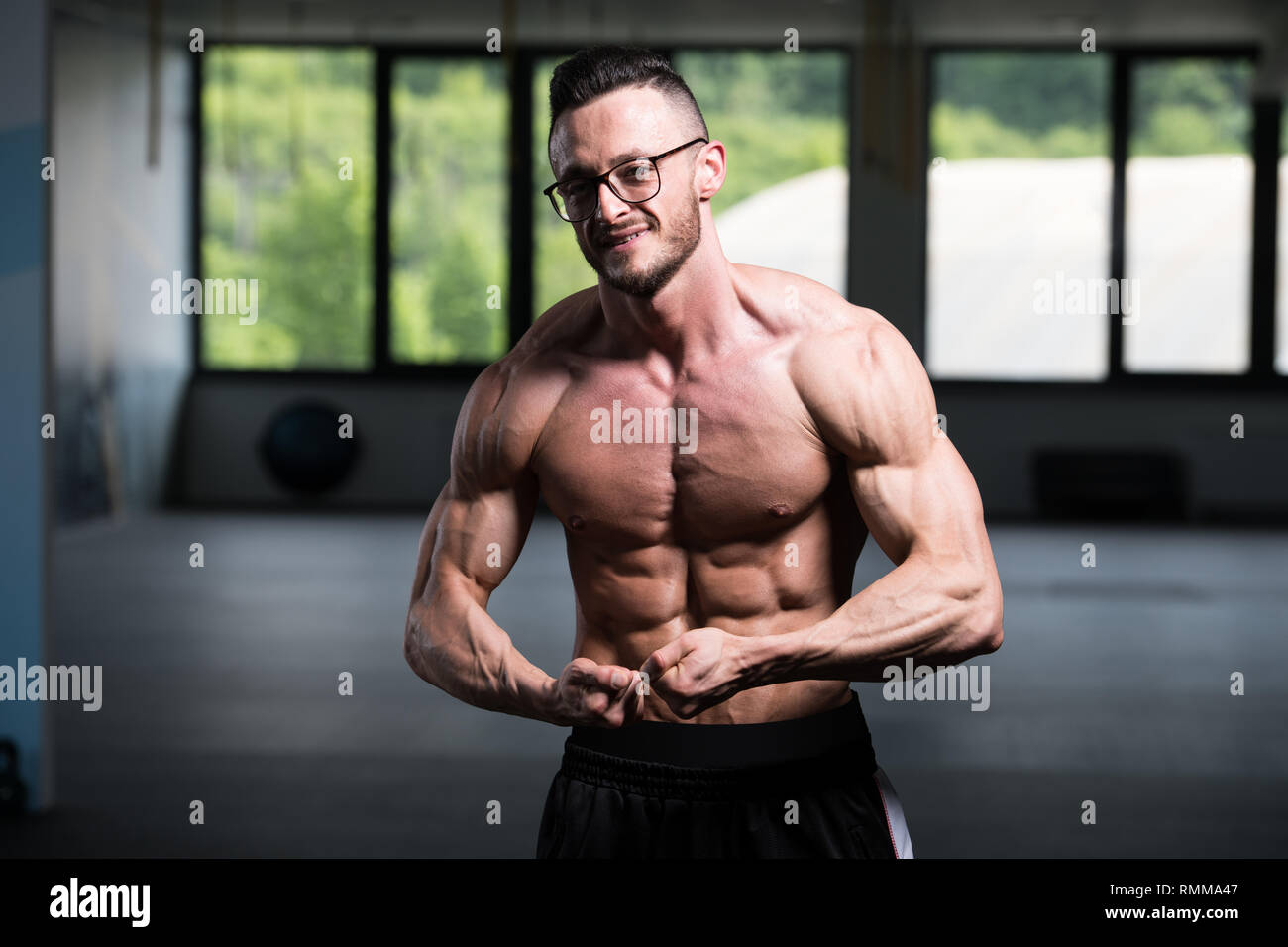 Handsome Geek Man Standing Strong In The Gym And Flexing Muscles ...