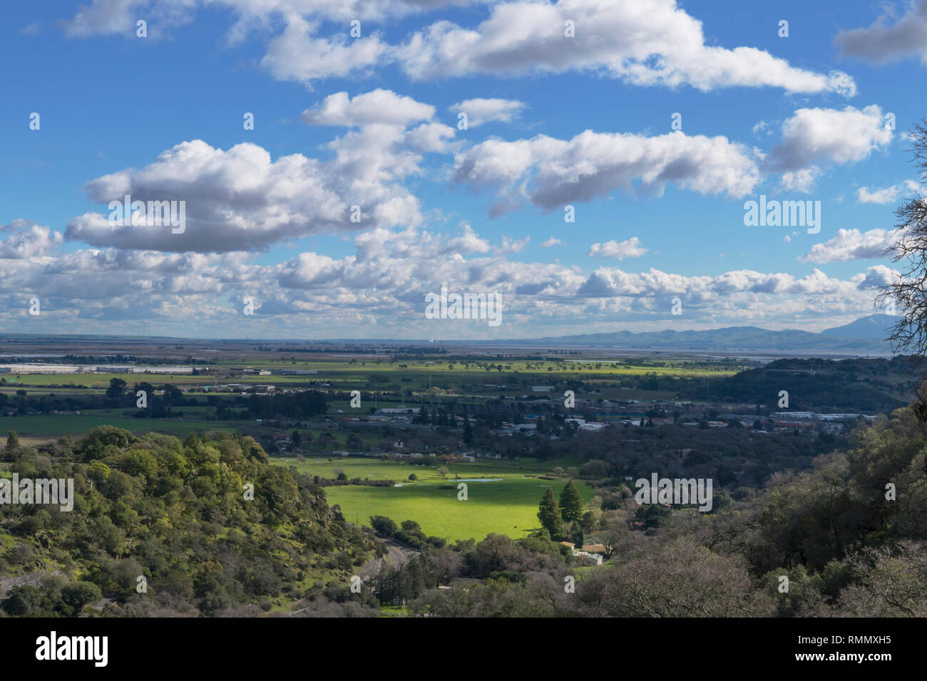 Landscape view from mountaintop, green sunlit valley with blue sky and ...