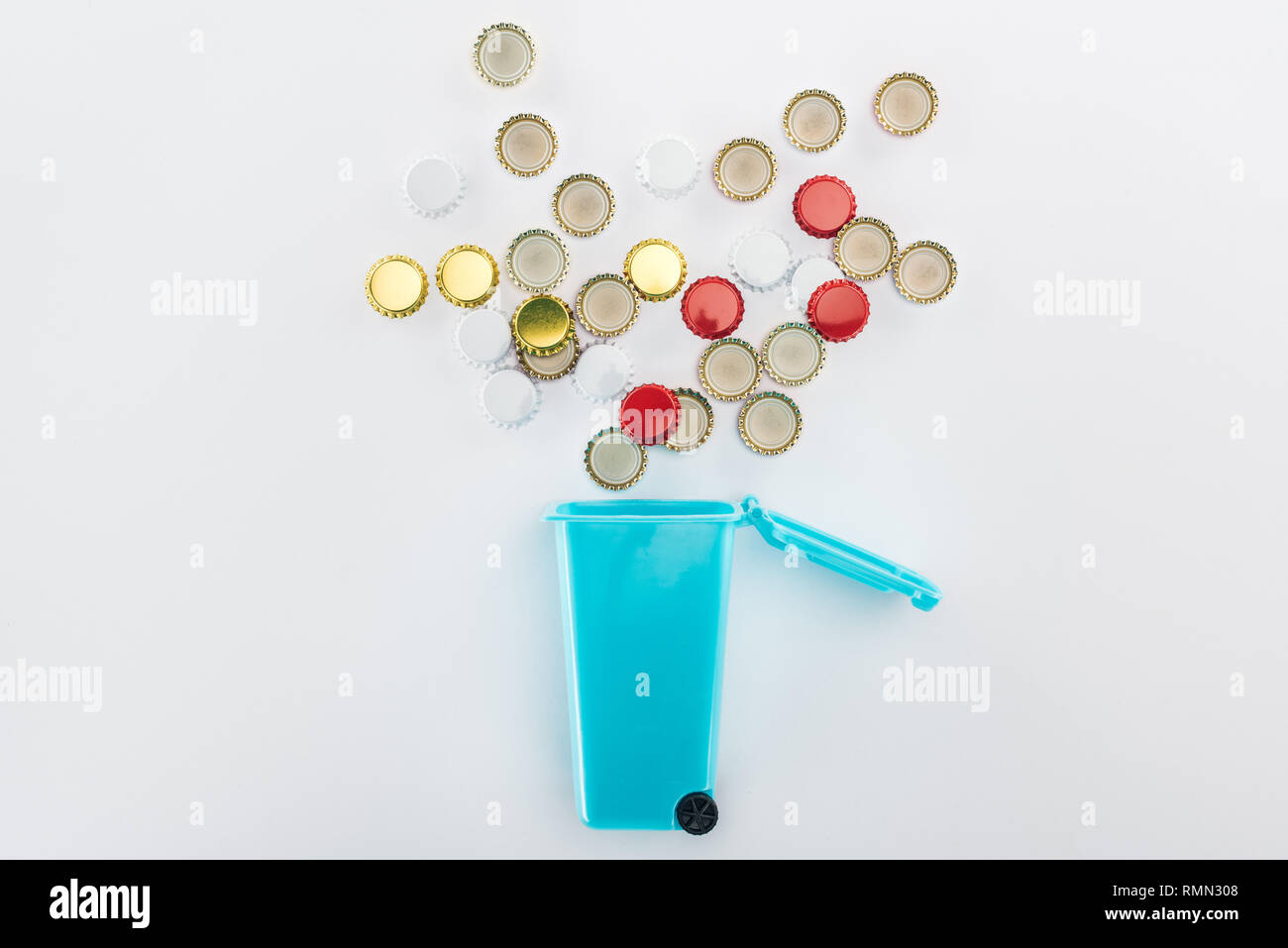 Top view of bottle caps falling down into blue toy trashcan on grey ...