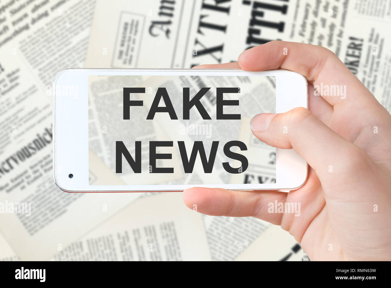 Fake news written on a computer smartphone screen, blurred newspapers ...