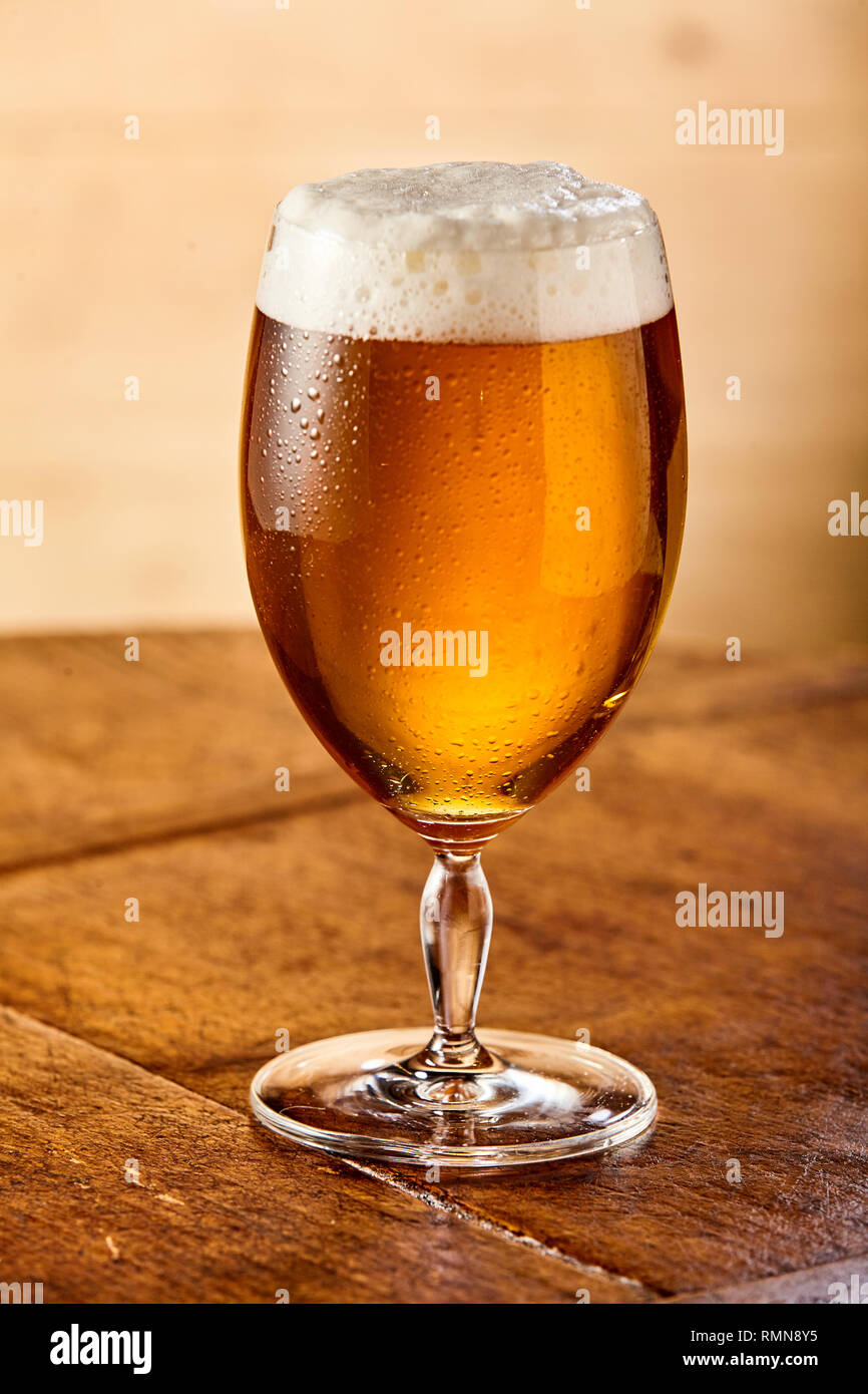 Chilled beer with a frothy head in a tall stemmed glass standing on an ...