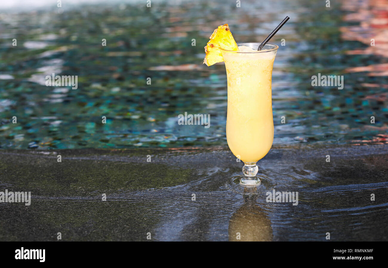 Glass of pinacolada cocktail standing on the swimming pool ledge in an ...