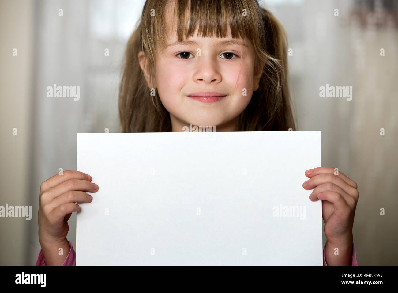 Happy smiling cute child girl holding white copy space sheet of drawing ...