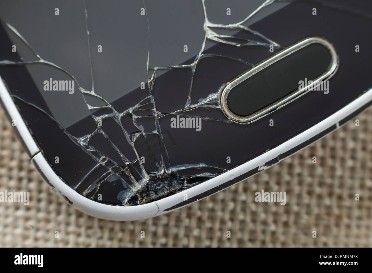 Close-up detail of black old cellphone with cracked screen on light ...